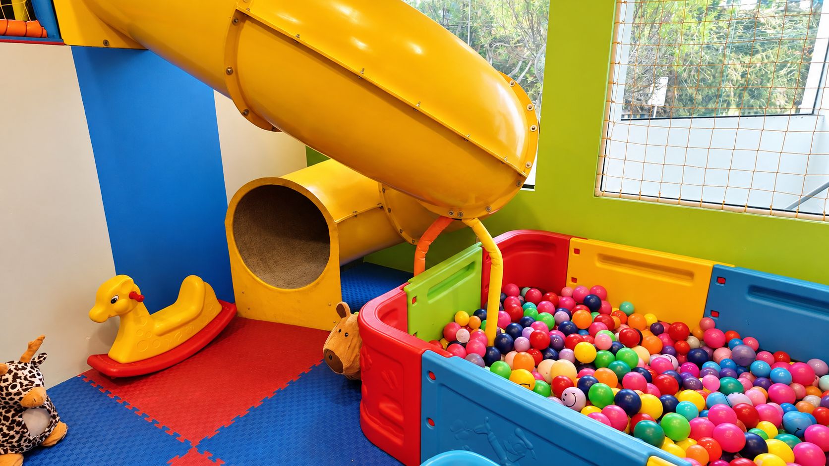 Espaço de recreação com escorrega, piscina de bolinhas e cantinho de atividades.