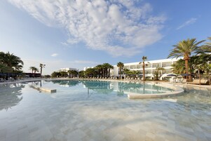 Uma piscina grande e convidativa, com espreguiçadeiras e palmeiras, cercada por edifícios modernos.