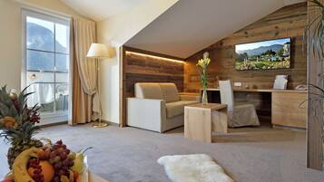 Uma sala de estar moderna com sofá, poltronas, mesa de centro e televisão montada numa parede de madeira. Uma janela grande com cortinas é visível, e uma fruteira está no chão.