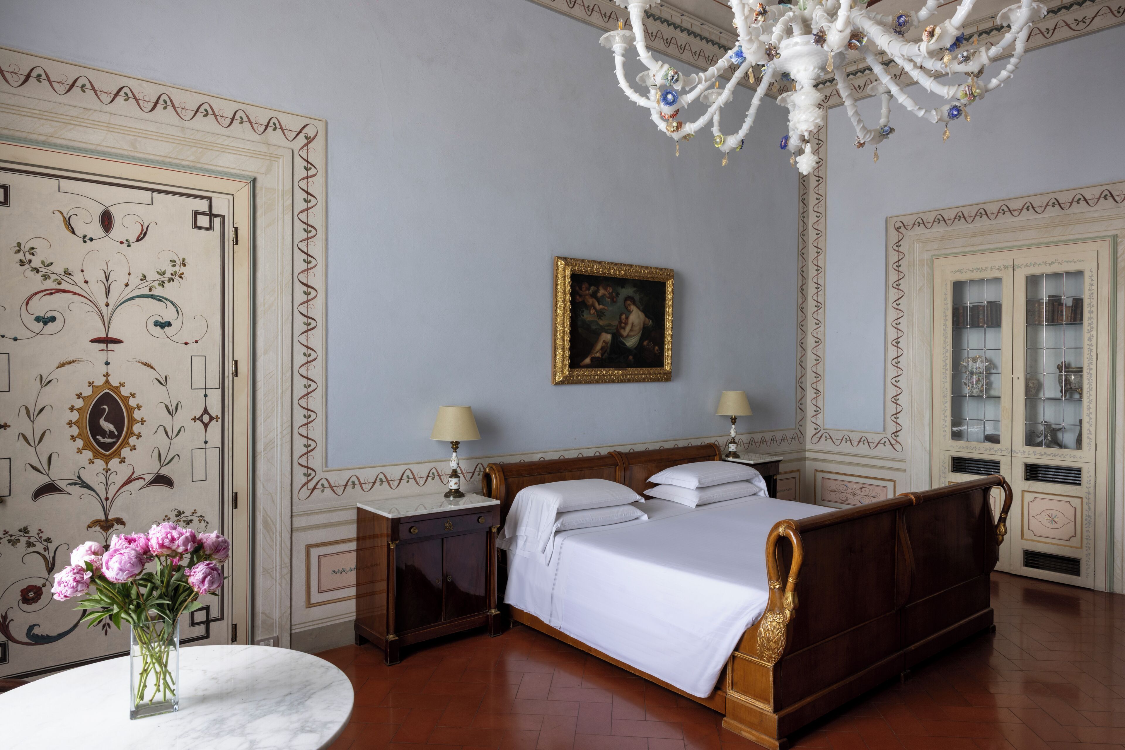 Quarto com cama, mesas de cabeceira, um candelabro, um quadro e uma porta decorativa.