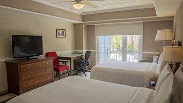 Quarto de hotel com duas camas, uma escrivaninha, televisão, uma cadeira, cômoda e janela com vista para o exterior.