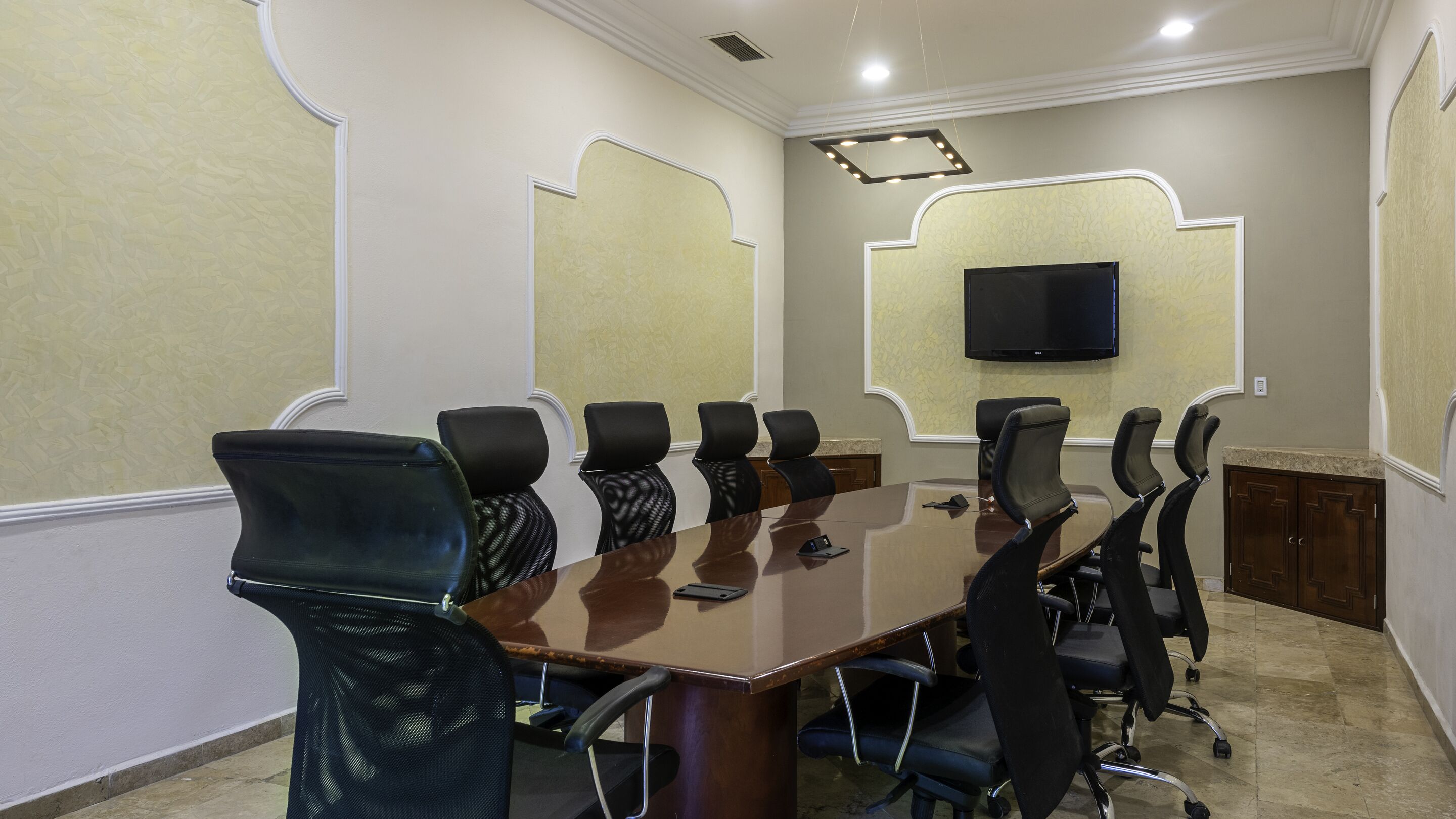 Uma sala de conferência com uma mesa comprida, várias cadeiras, uma TV de tela plana e um painel decorativo na parede.