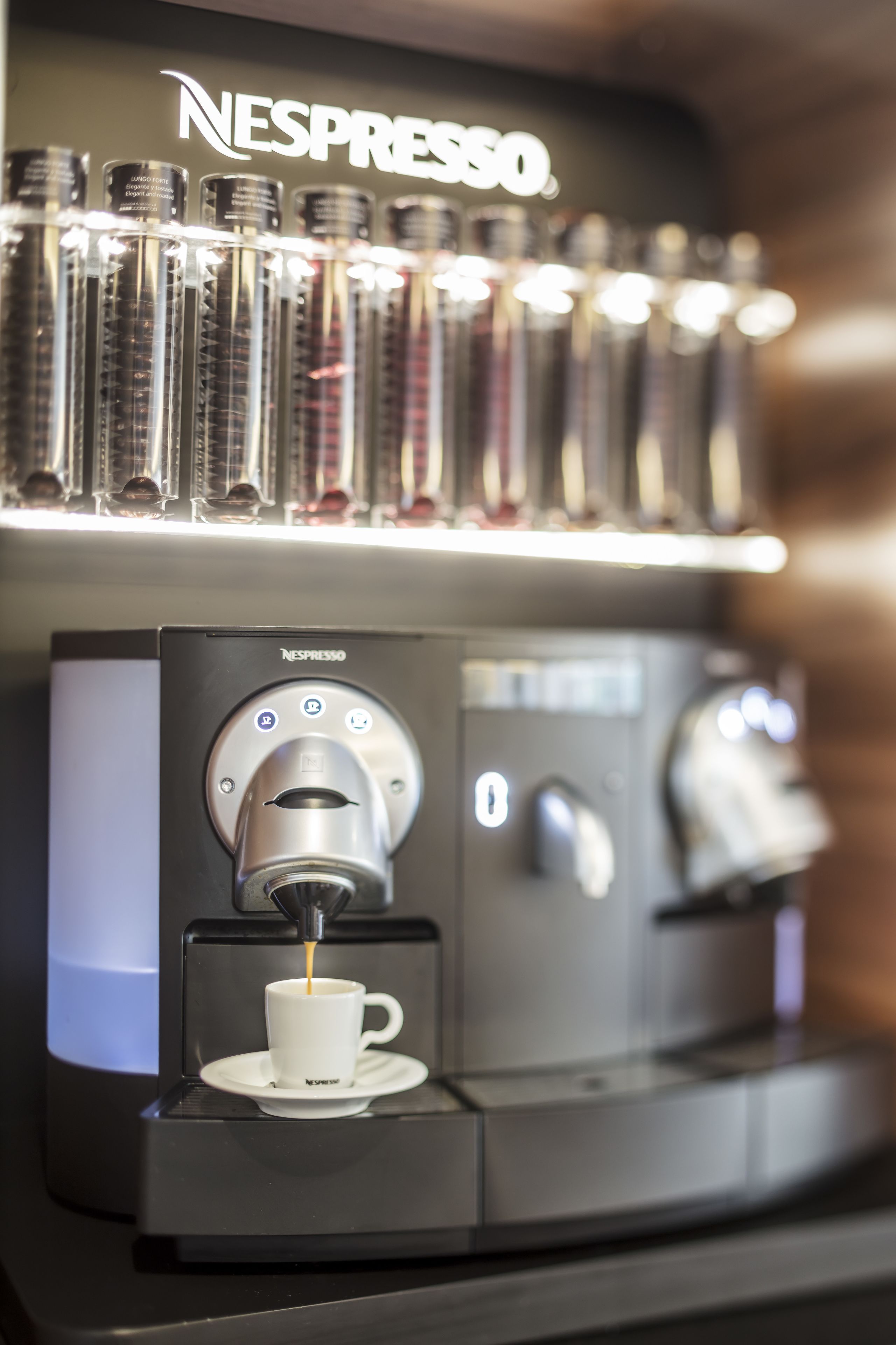 Máquina de café Nespresso com vários pódios de café e uma chávena a ser dispensada.