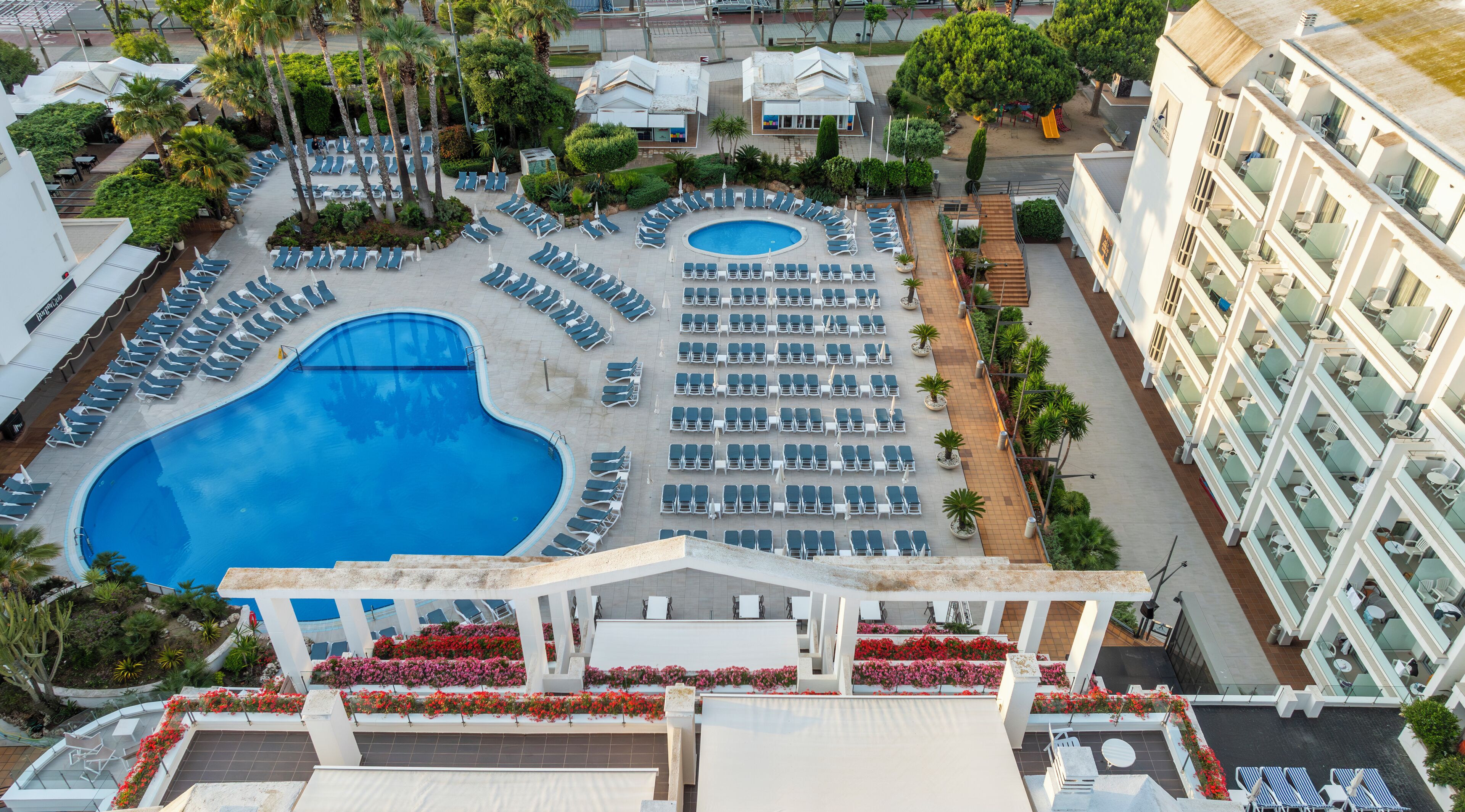 Um resort com uma grande piscina, diversas áreas de descanso e vários arranjos de assentos ao ar livre.
