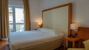 Quarto de hotel com uma cama grande, duas luminárias de cabeceira, um telefone ao lado da cama e vista para a varanda.