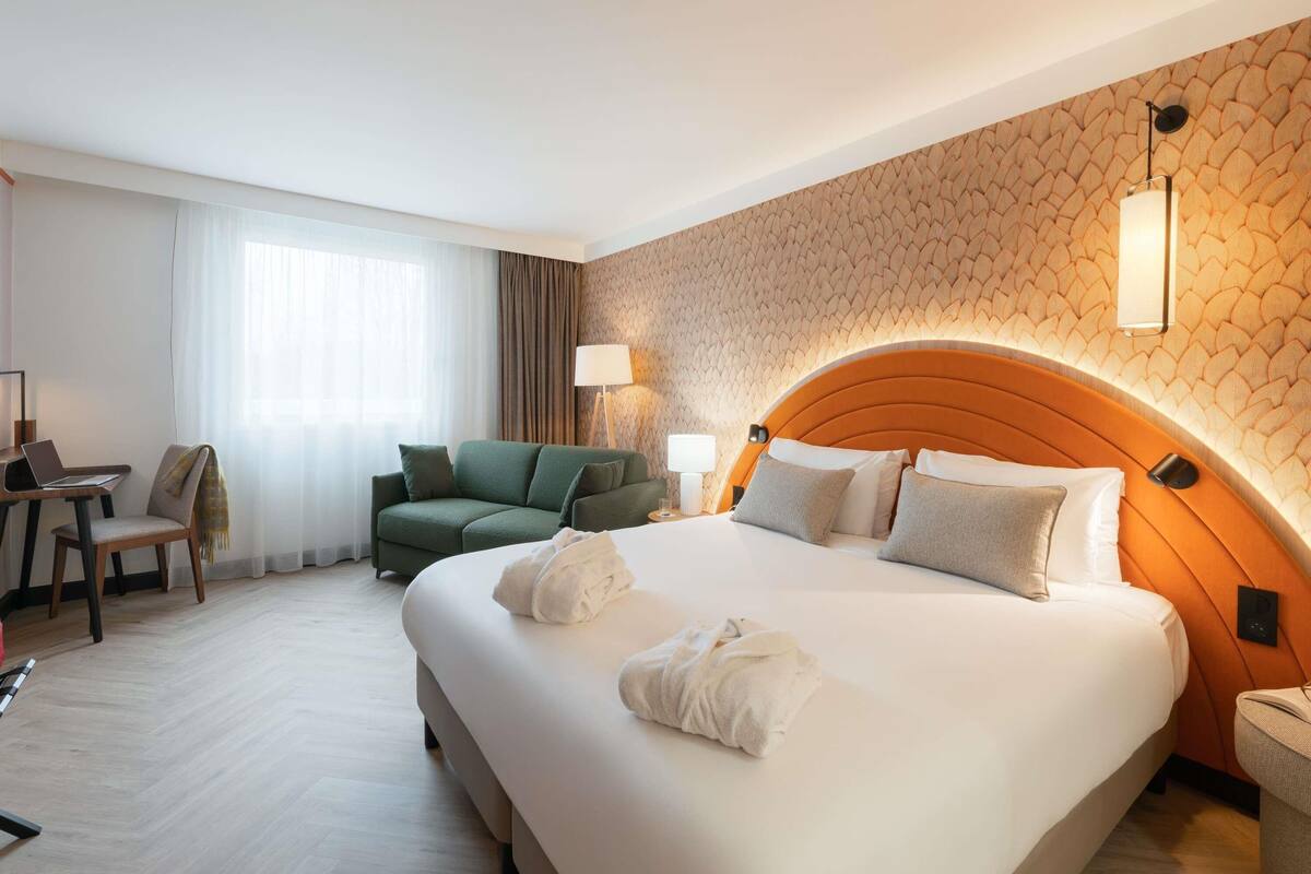 Quarto de hotel com uma cama grande, uma escrivaninha, um sofá verde e uma parede com padrão texturizado.