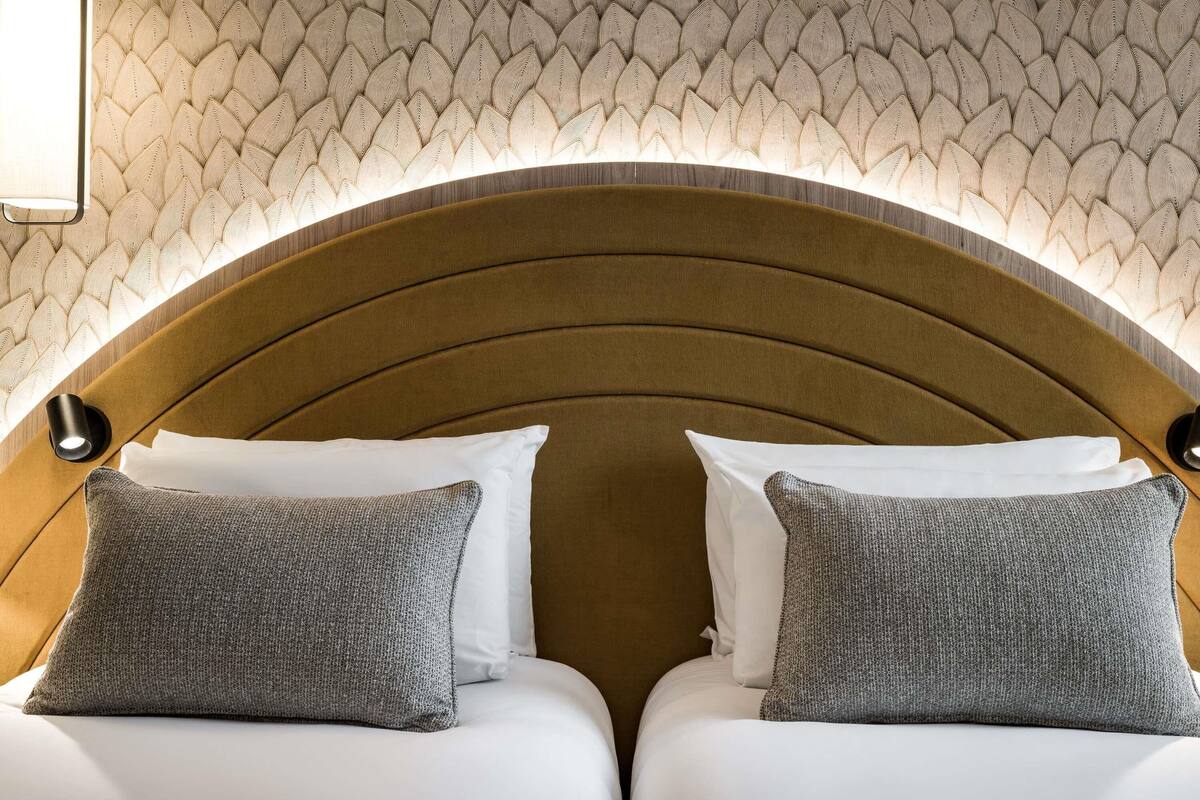 Cama de casal com cabeceira, duas almofadas e parede com padrão texturizado.