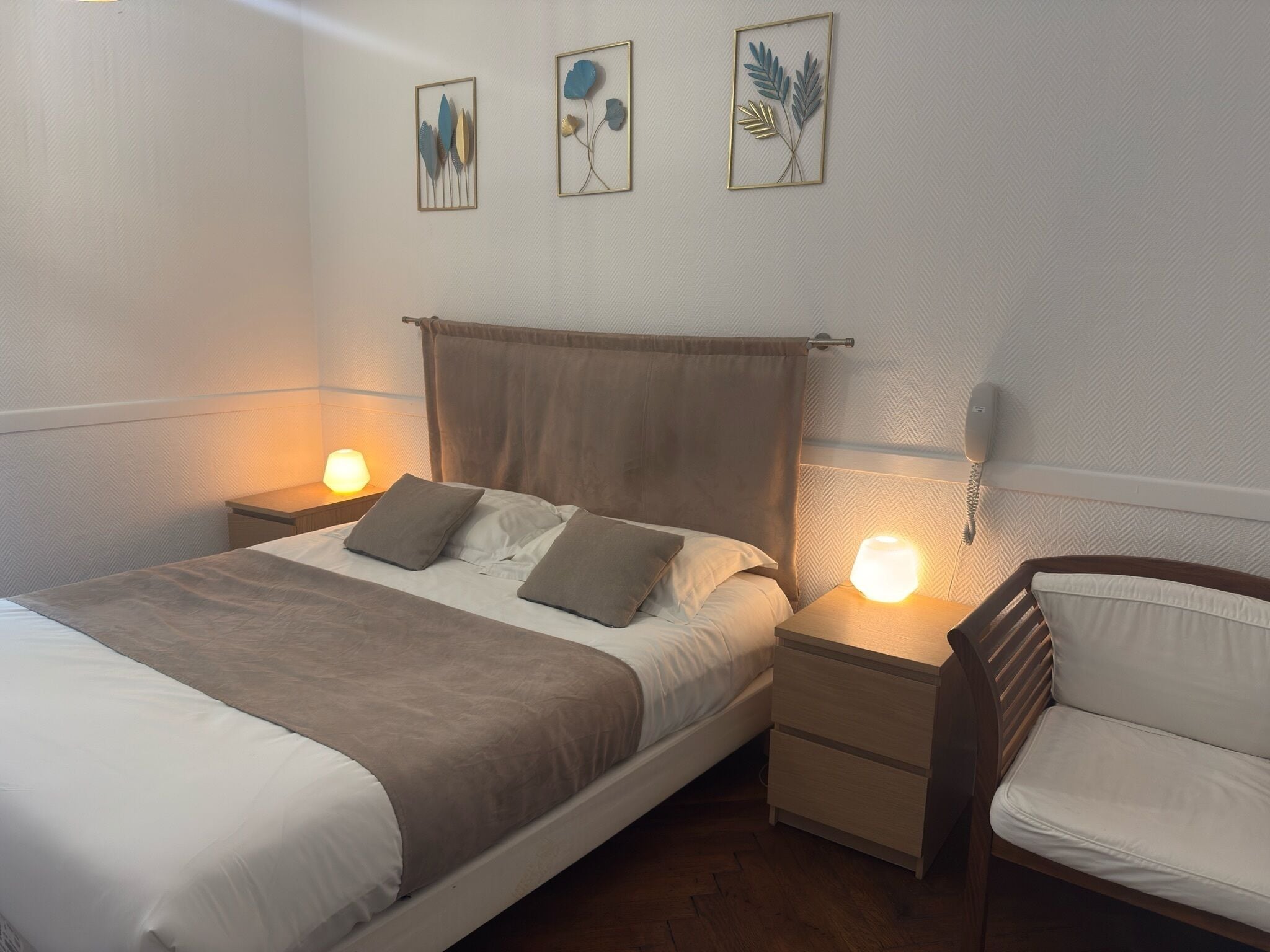 Quarto com cama, mesas de cabeceira, um banquinho, cadeira e obra de arte na parede.