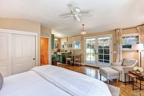 Quarto com cama grande, ventoinha no teto, área de refeições com cadeiras e vista para o exterior.