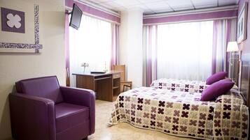 Quarto de hotel com cama, escrivaninha, cadeira e televisão.