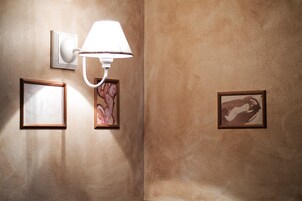 Paredes com três obras de arte emolduradas e uma luminária de parede.