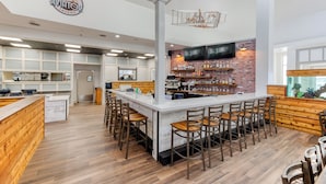 Uma área de bar moderna com um balcão comprido, vários bancos e uma parede de destaque em tijolos.