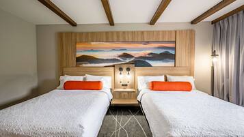 Quarto de hotel com duas camas, uma pintura grande na cabeceira e uma mesinha de cabeceira com luzes.