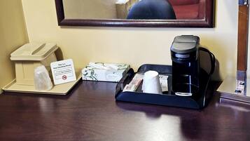 Quarto de hotel com aviso de proibido fumar, um cesto de lixo, um tabuleiro com cafeteira, uma caixa de lenços e uma embalagem de lenços.