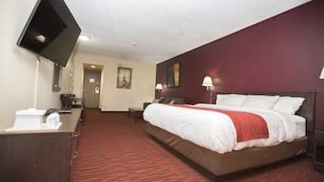 Quarto de hotel com uma cama grande, uma mesa com televisão de tela plana, uma cadeira e uma luminária de mesa.