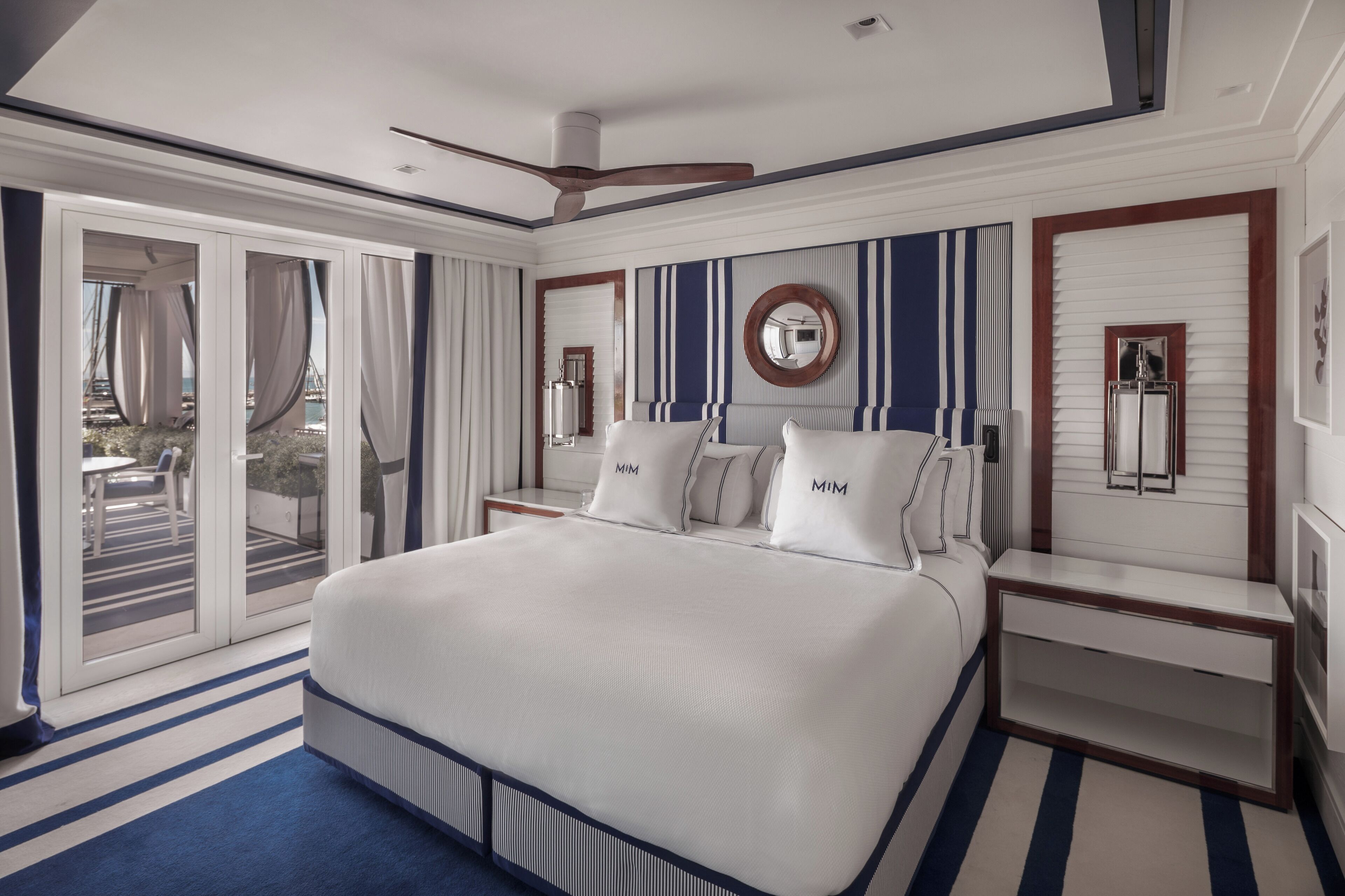 Quarto de hotel com cama grande, ventilador de teto, vista para a praia e chão listrado.