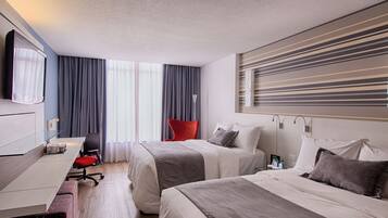 Quarto de hotel com duas camas, uma escrivaninha, uma cadeira e uma televisão.