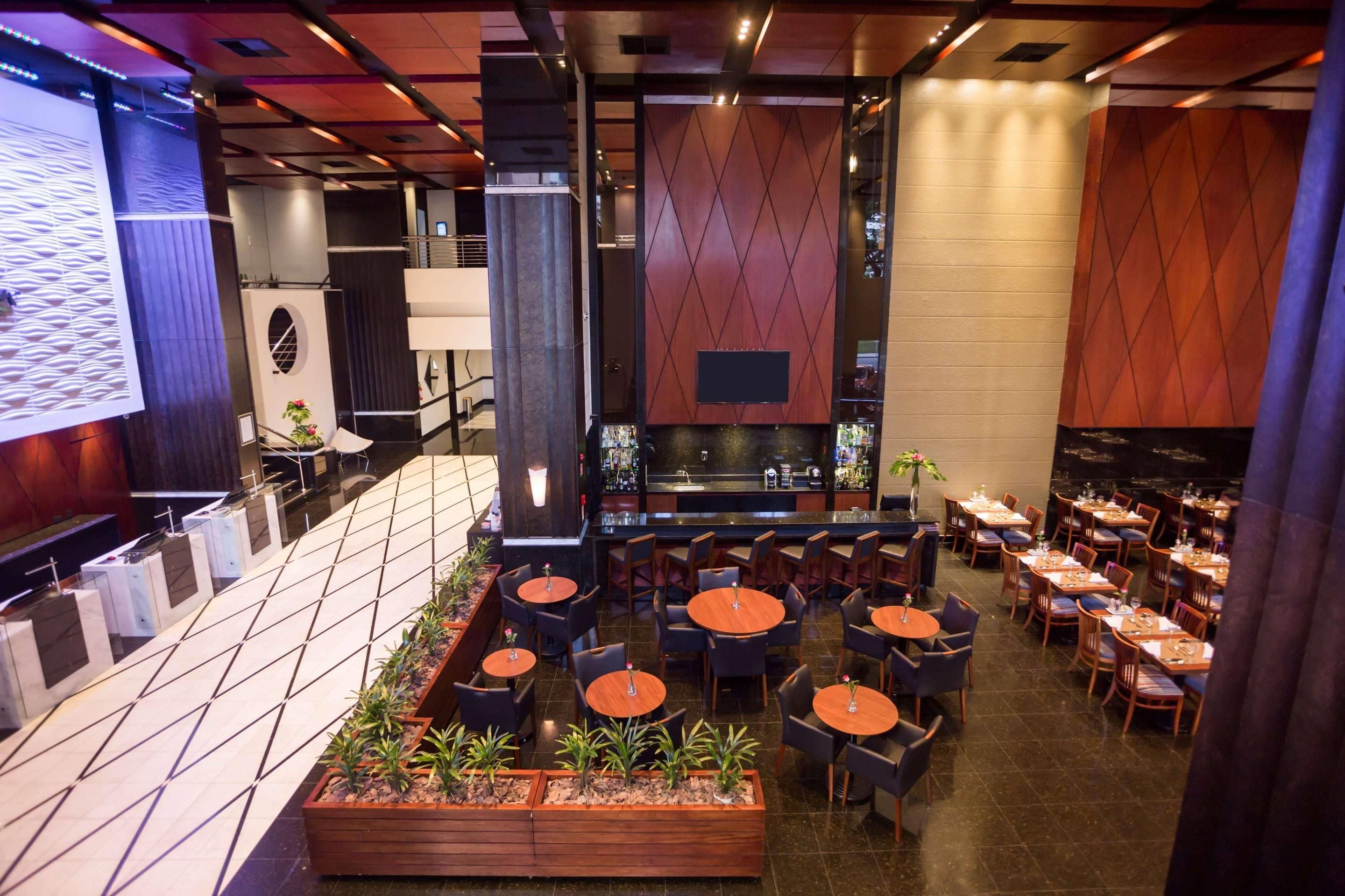 Restaurante com área de bar, diversos arranjos de assento e parede decorativa com padrão geométrico.