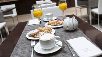 Uma mesa posta para o café da manhã, com croissants, uma xícara de café e dois copos de suco de laranja.