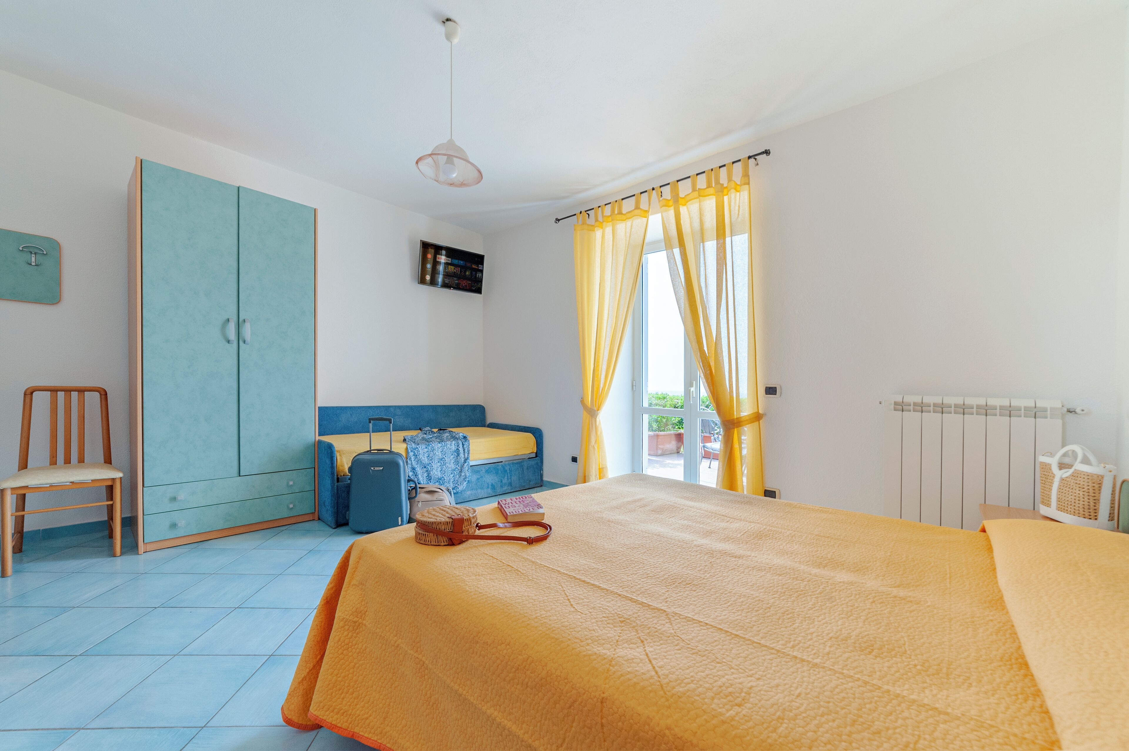 Um quarto com uma cama, um guarda-roupa, uma cadeira, uma mala e um radiador.