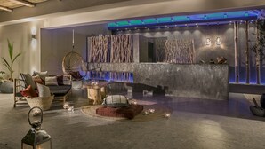 Um lobby moderno com balcão de recepção, área de estar e elementos decorativos como plantas e iluminação.