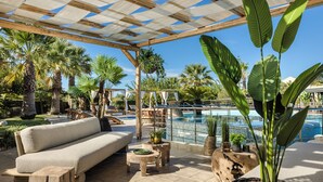 Uma área externa coberta com piscina, móveis de madeira e diversos vasos de plantas.