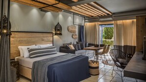 Quarto de hotel moderno com uma cama grande, um sofá, uma mesa de jantar e uma cadeira. Há uma janela com cortinas e vista para o verde lá fora.