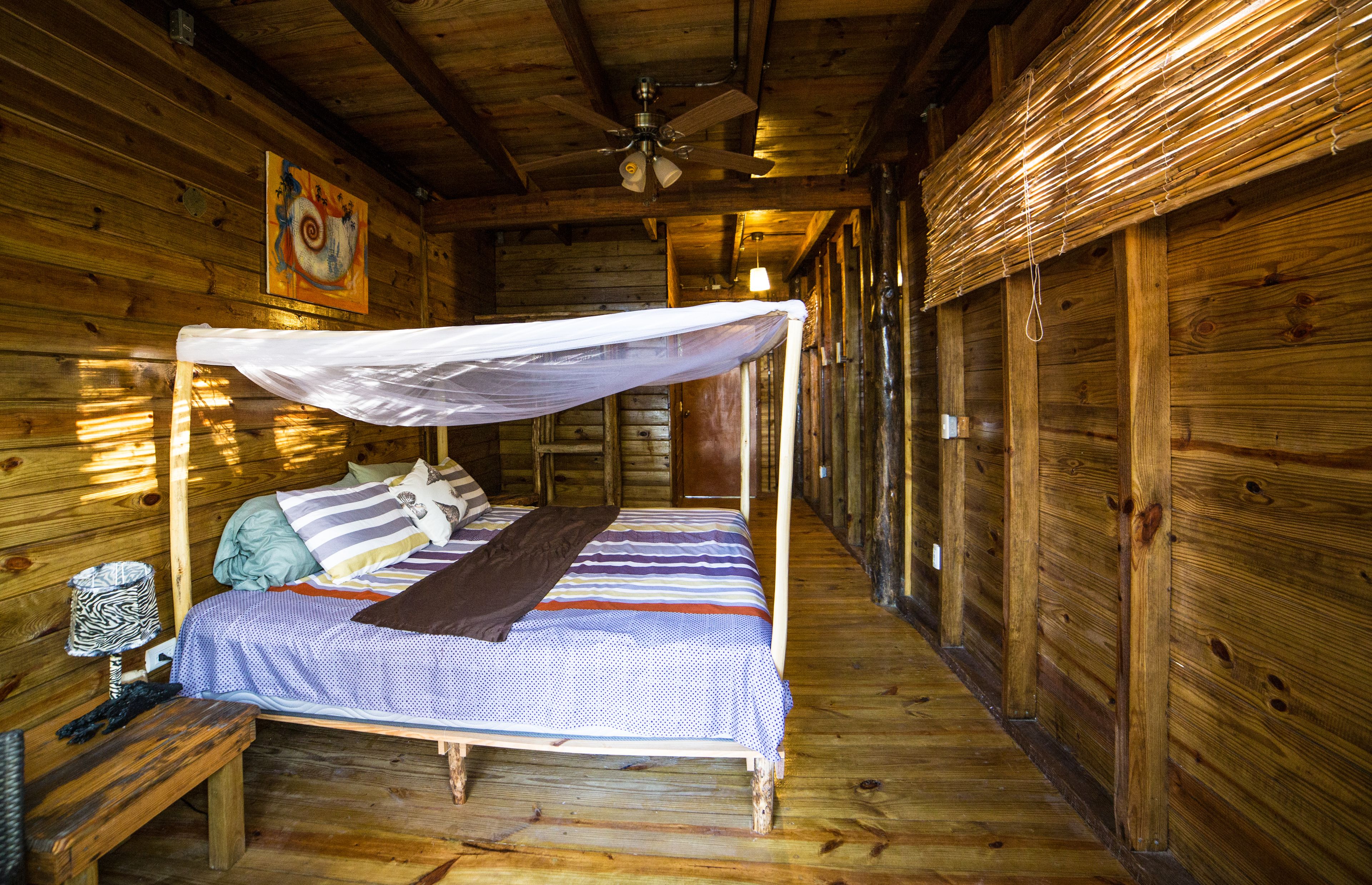 Quarto de cabana de madeira com cama, ventoinha no teto e piso de madeira.