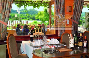 Restaurante com mesa posta para refeição, vista para um lago e montanha ao fundo.