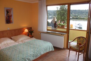 Quarto com cama, uma cadeira, janela com vista para um rio e radiador.