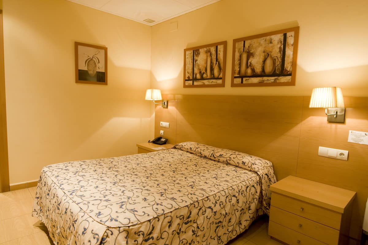 Quarto de hotel com cama, mesas de cabeceira, luminárias e obras de arte na parede.