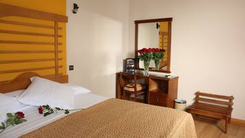 Quarto de hotel com cama, escrivaninha, cadeira, banco e espelho.