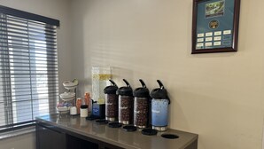 Uma estação de bebidas com dosadores para café, chá e água, e um prêmio emoldurado na parede.