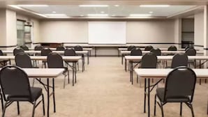 Uma sala de conferências com fileiras de mesas e cadeiras, um quadro branco e uma tela de projeção.