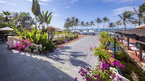 Um resort tropical com um caminho pavimentado, palmeiras e guarda-sóis de praia.