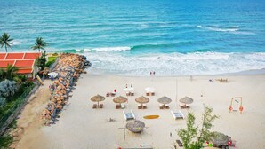 Uma praia com guarda-sóis, espreguiçadeiras e uma costa rochosa.