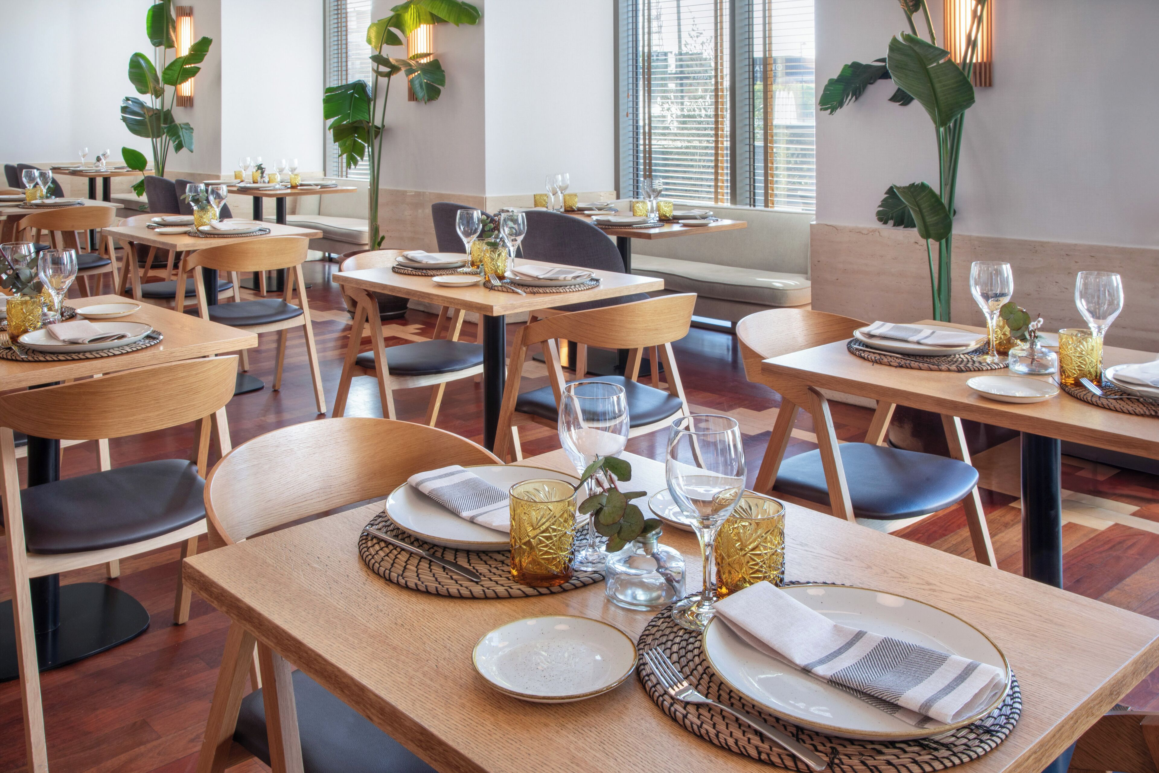 Um restaurante com várias mesas preparadas para refeições, com mobiliário de madeira e design de interiores moderno.