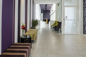 Um hall de hotel moderno com um balcão de recepção longo, área de estar e escada que leva a um andar superior.