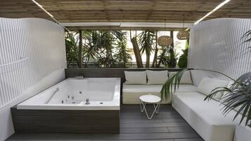 Uma área de spa moderna ao ar livre, com hidromassagem, um sofá branco e uma pequena mesa.