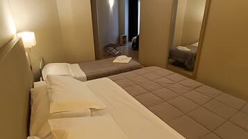 Quarto de hotel com duas camas, uma mesa de cabeceira, um abajur e um espelho.