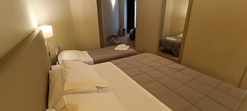Quarto de hotel com duas camas, uma mesa de cabeceira, um abajur e um espelho.
