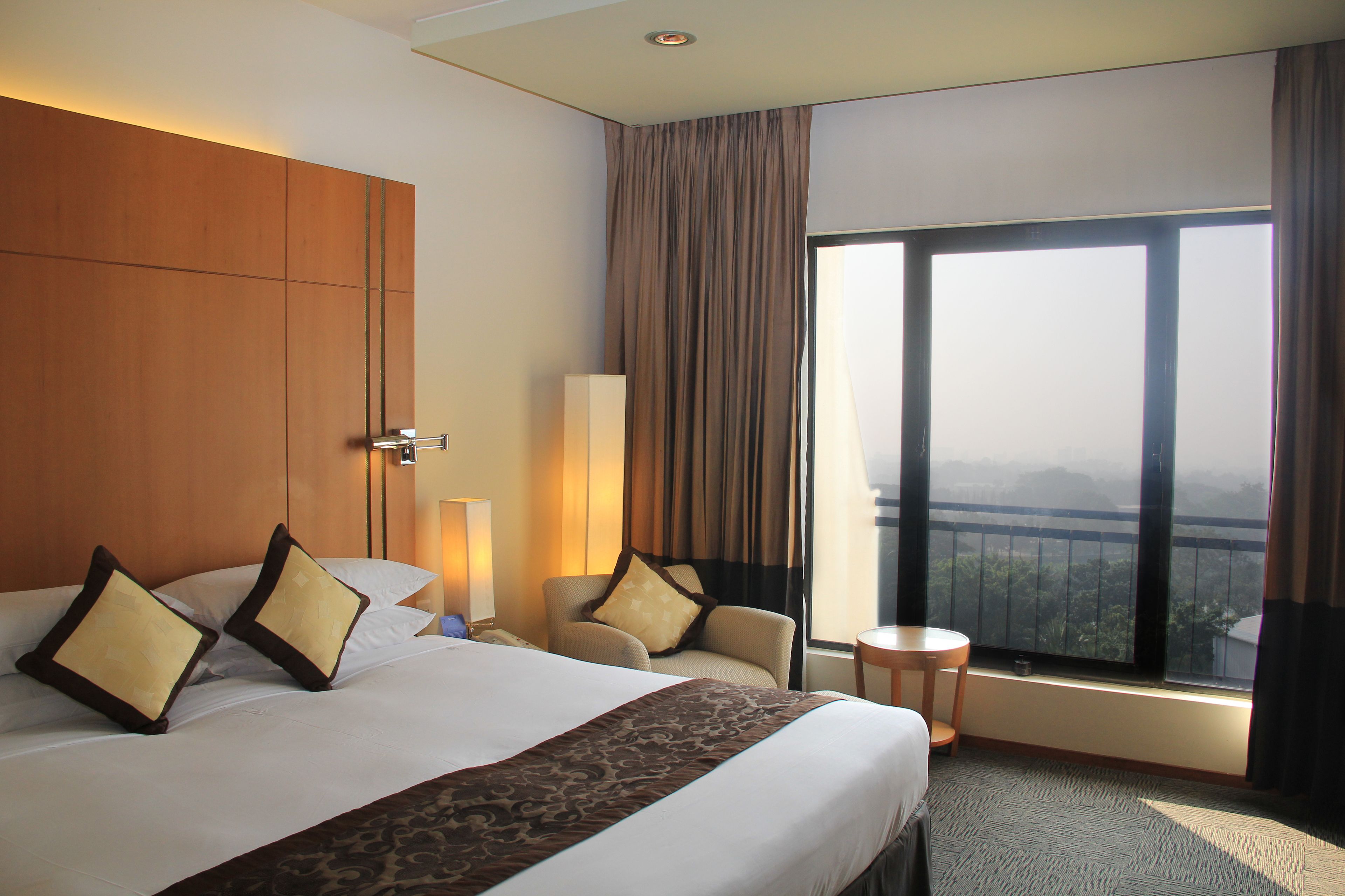 Quarto de hotel com uma cama grande, uma cadeira, uma mesinha e uma janela com vista.