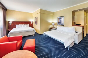 Quarto de hotel com duas camas, uma escrivaninha e uma cadeira vermelha.