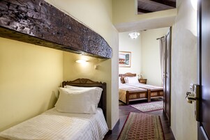 Um corredor estreito conduz a um quarto com cabeceira de madeira, cama com roupa de cama branca e porta com fechadura moderna.
