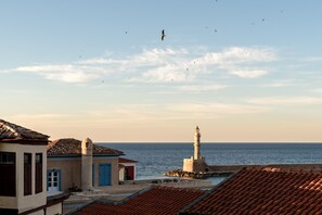 Uma vila costeira com um farol, edifícios com telhados de terracota e uma vista clara do mar.
