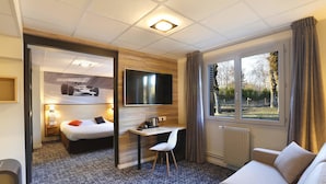 Quarto de hotel com cama, escrivaninha, cadeira, televisão e janela com cortinas.