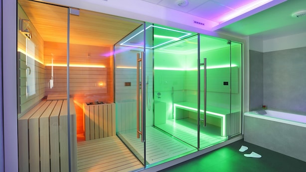 Um spa moderno com ambiente iluminado em verde, uma estrutura de vidro, bancos de madeira.