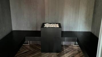 Quarto moderno e minimalista com piso de madeira em padrão herringbone, um banco preto e uma pequena mesa com um objeto branco.