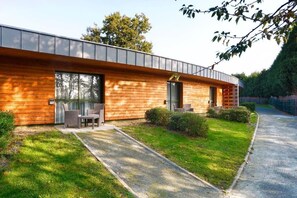 Uma casa moderna com fachada de madeira, um caminho de entrada pavimentado e um pequeno alpendre com móveis para área externa.