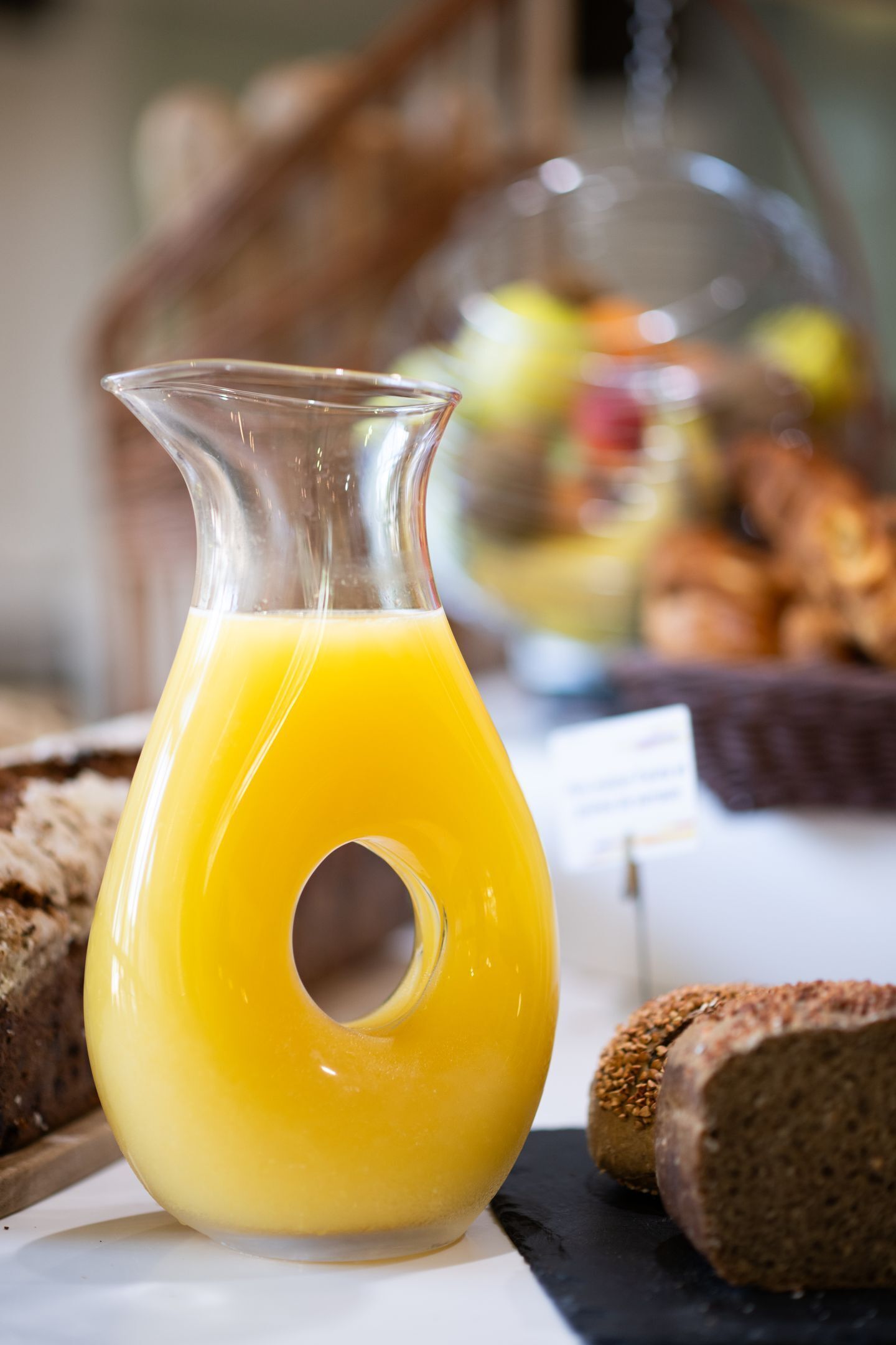 Um jarro de vidro transparente com suco de laranja sobre uma mesa, junto com fatias de pão.